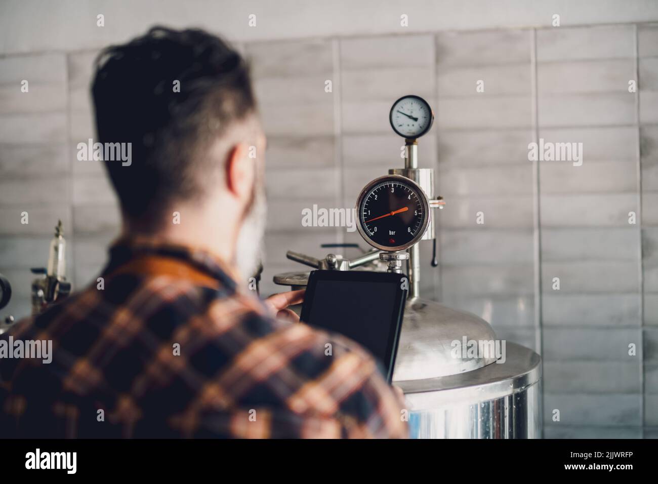 Man is working at craft beer factory. He is operating machinery in ...