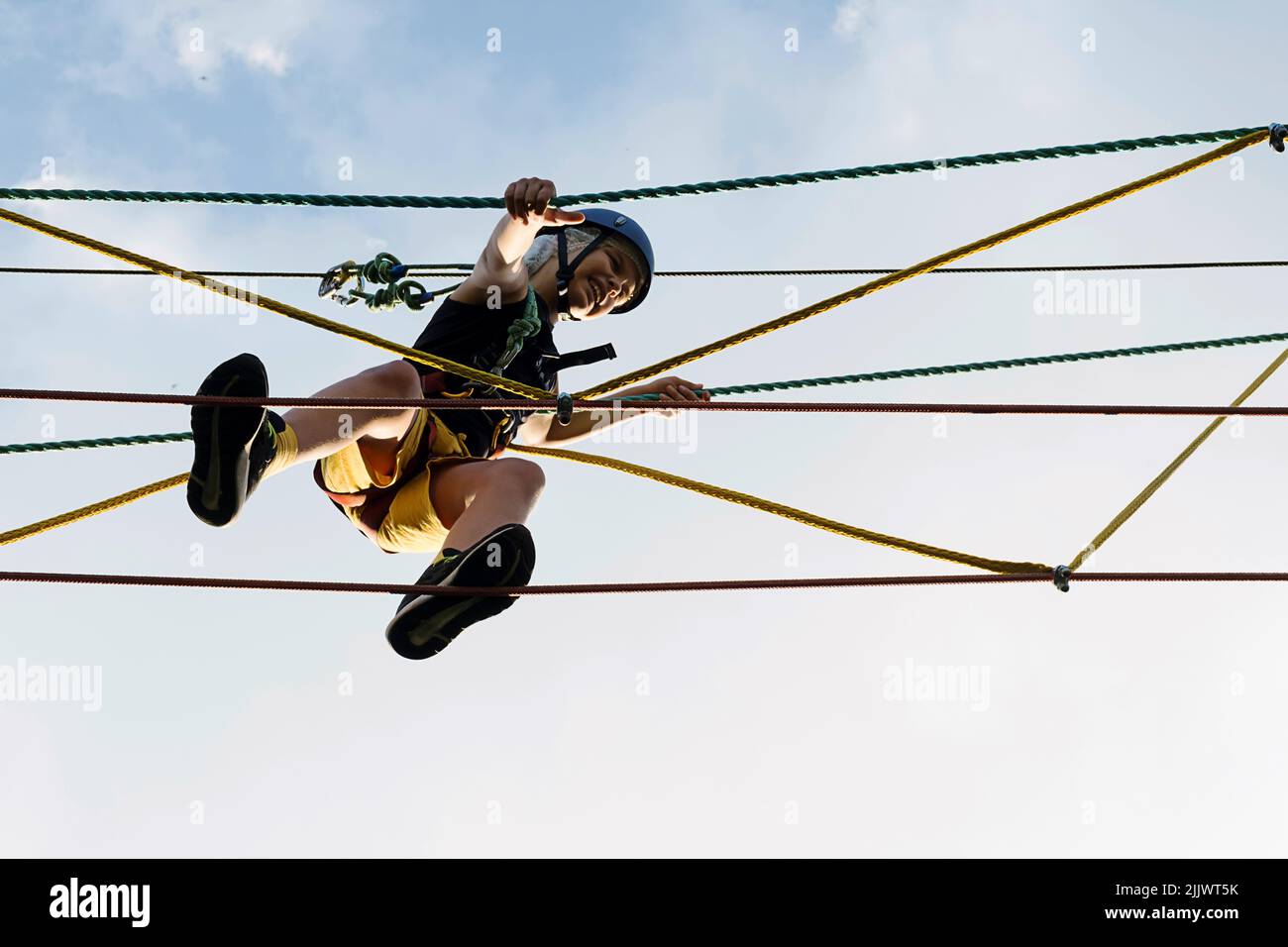 Child in safety harness and helmet in rope park. Boy climbs attached ...