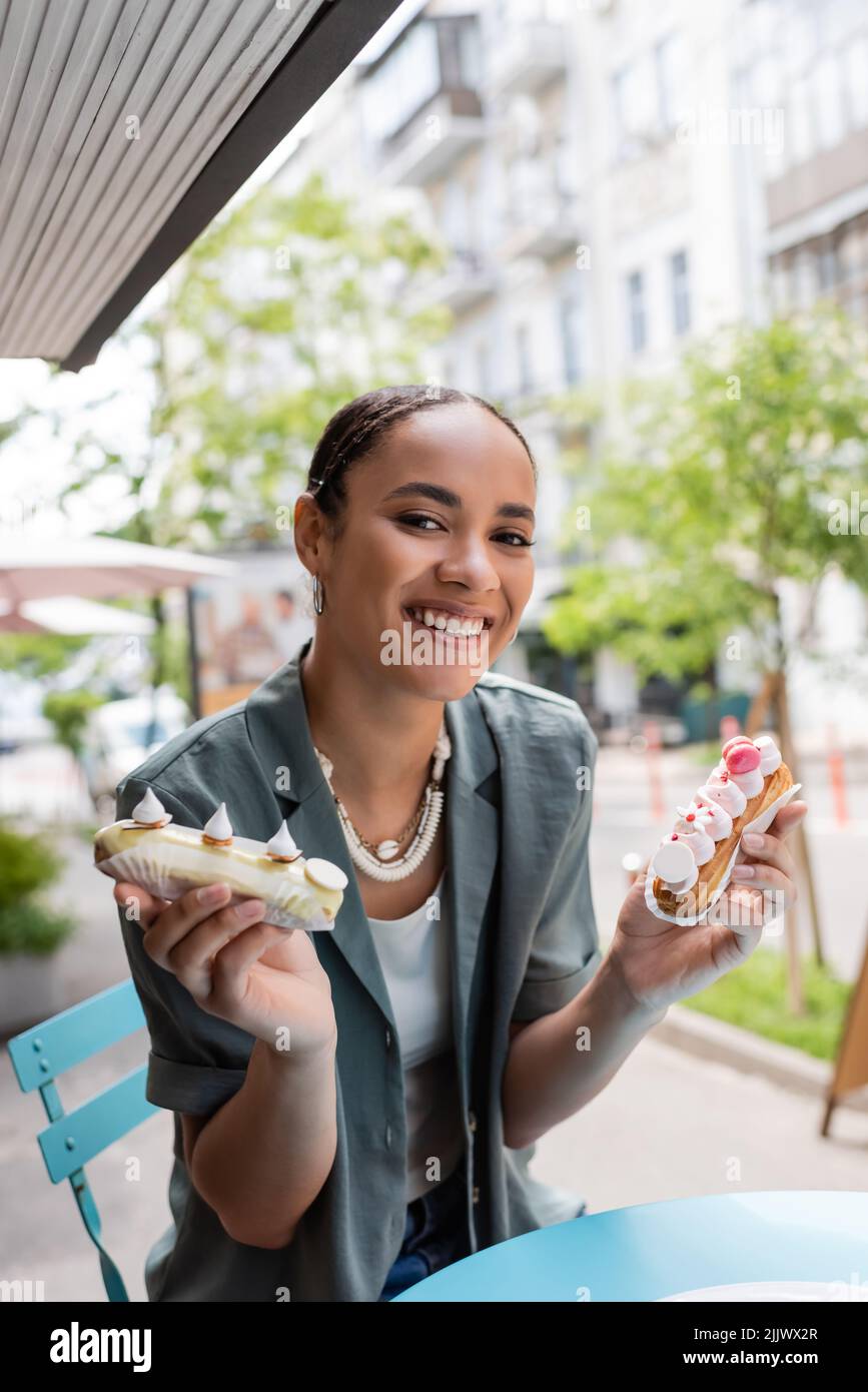Smiling african american client holding eclairs and looking at camera ...