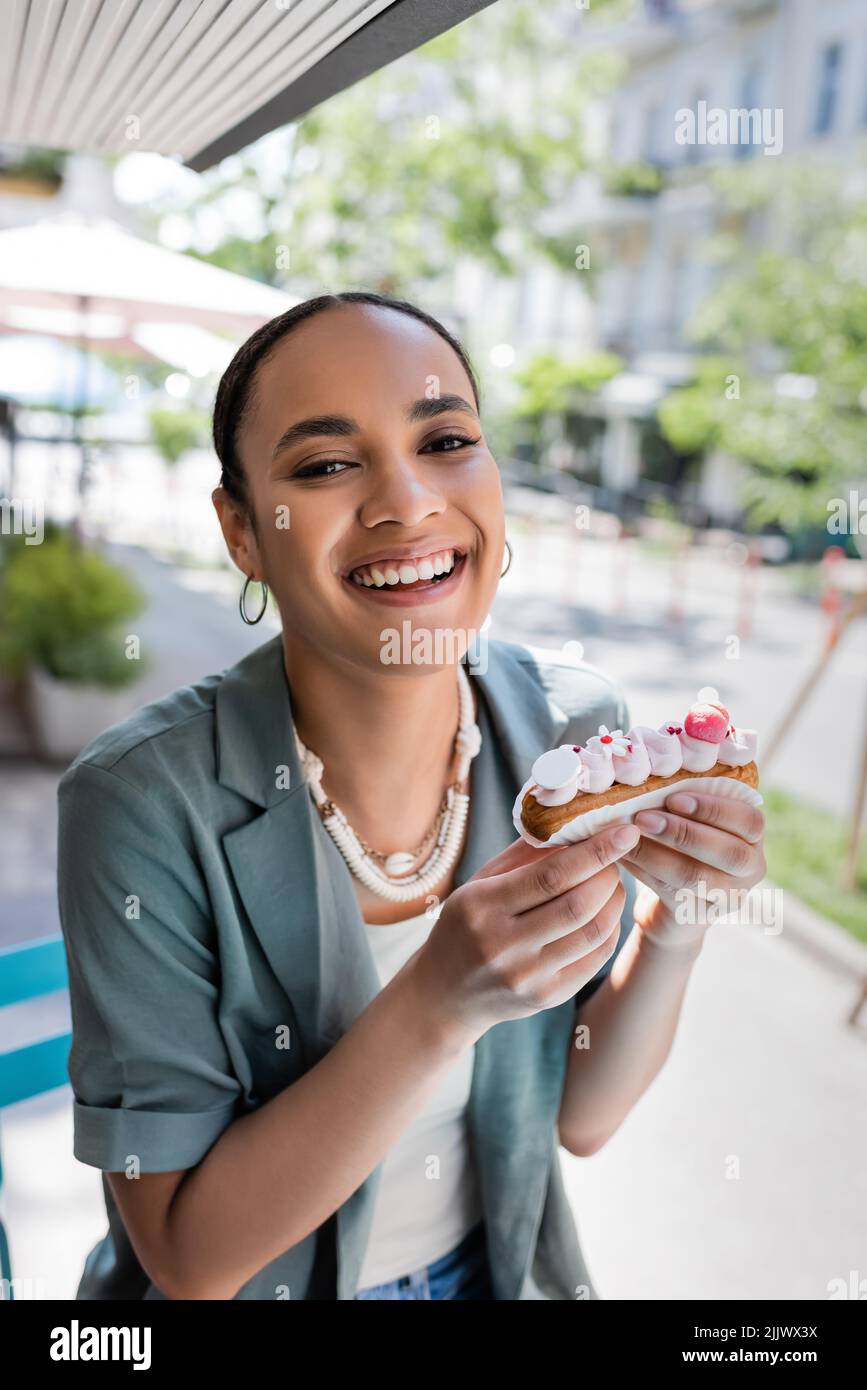 Positive african american client holding tasty eclair on terrace of ...