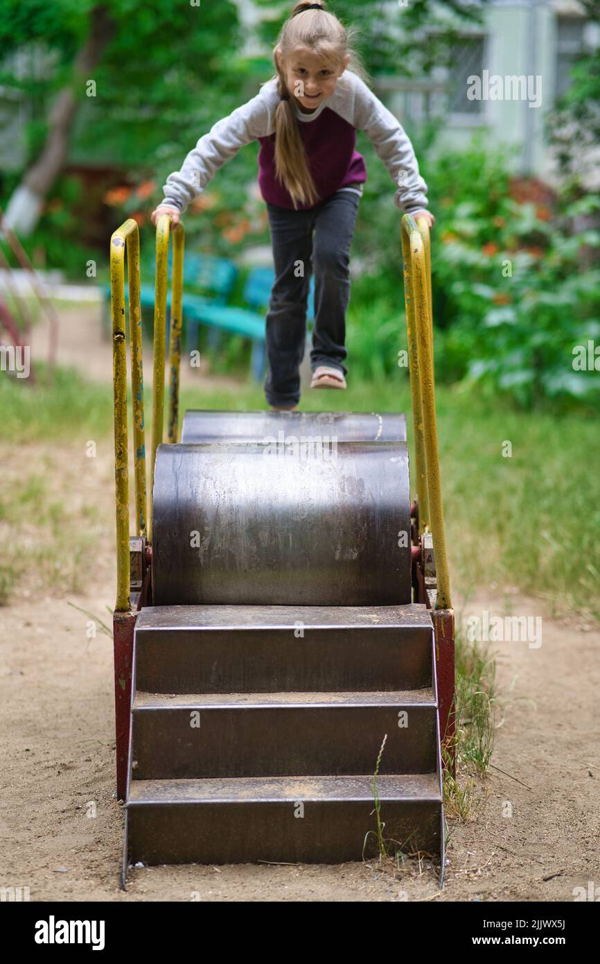 Cute blond girl playing on an old soviet-era playground, running over t ...