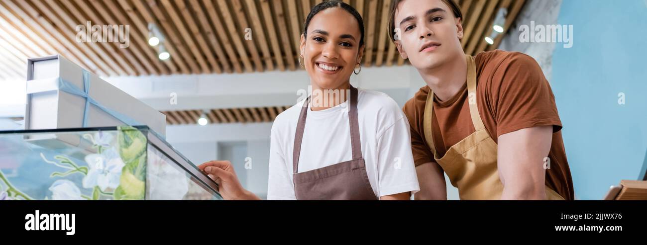 Positive multiethnic workers of sweet shop looking at camera, banner ...