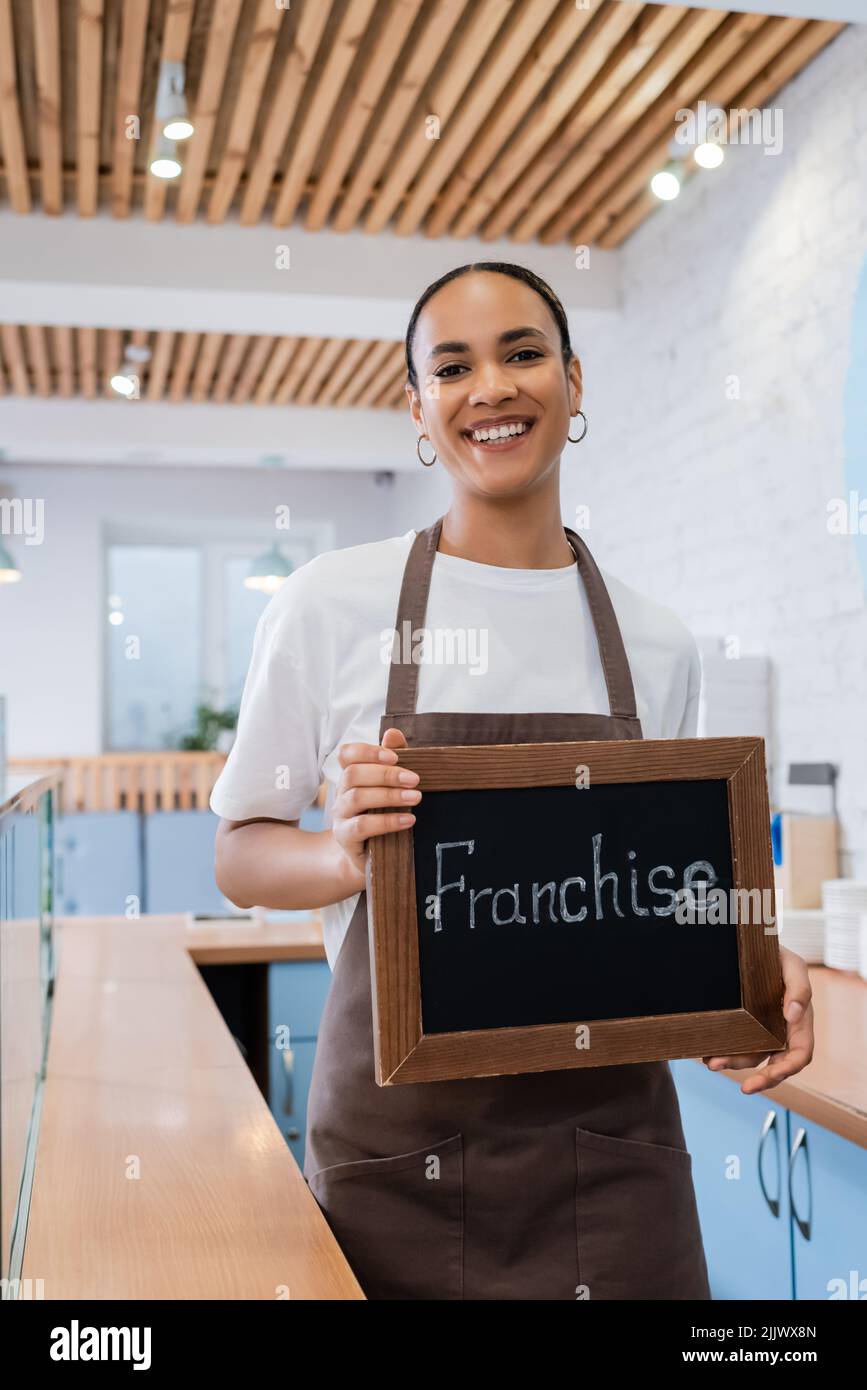 Positive african american barista holding chalkboard with franchise ...