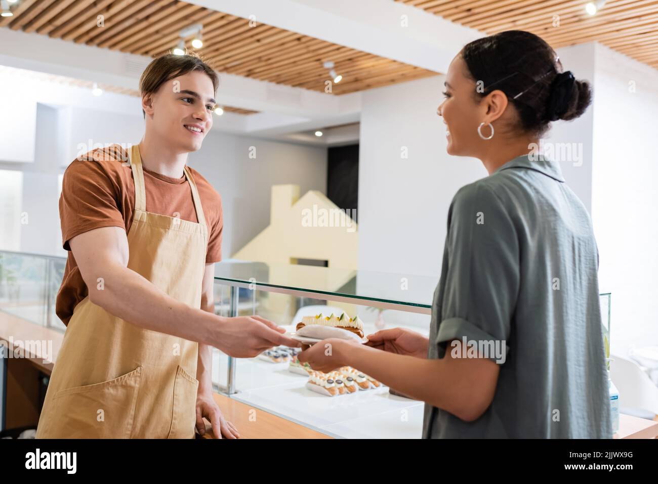 Positive seller giving dessert to african american client in sweet shop ...
