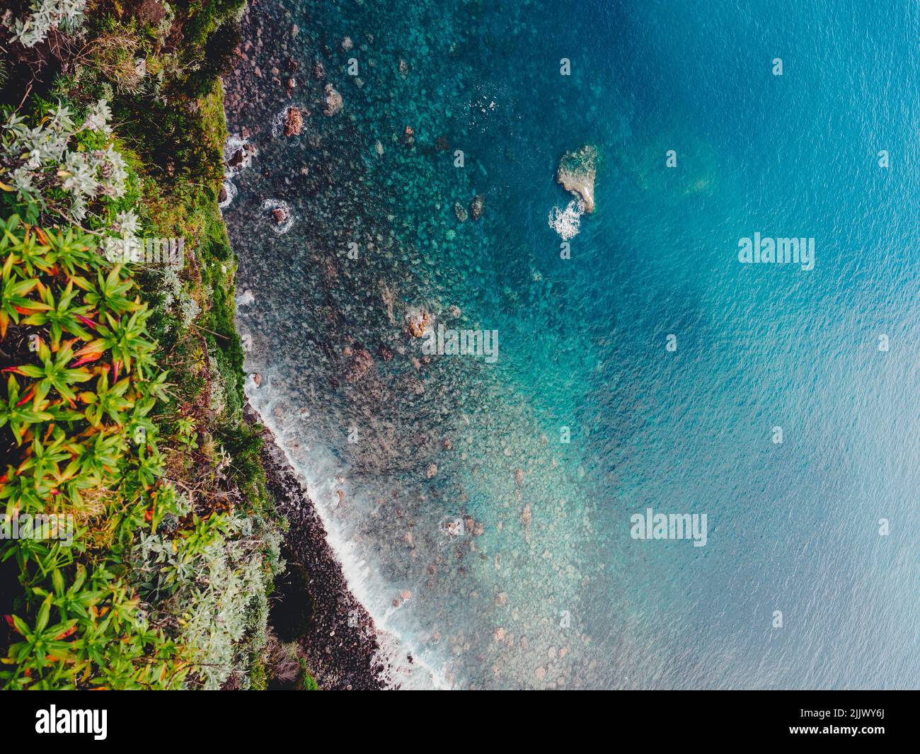 A top view of blue sea water from forested cliffs on the coast of ...