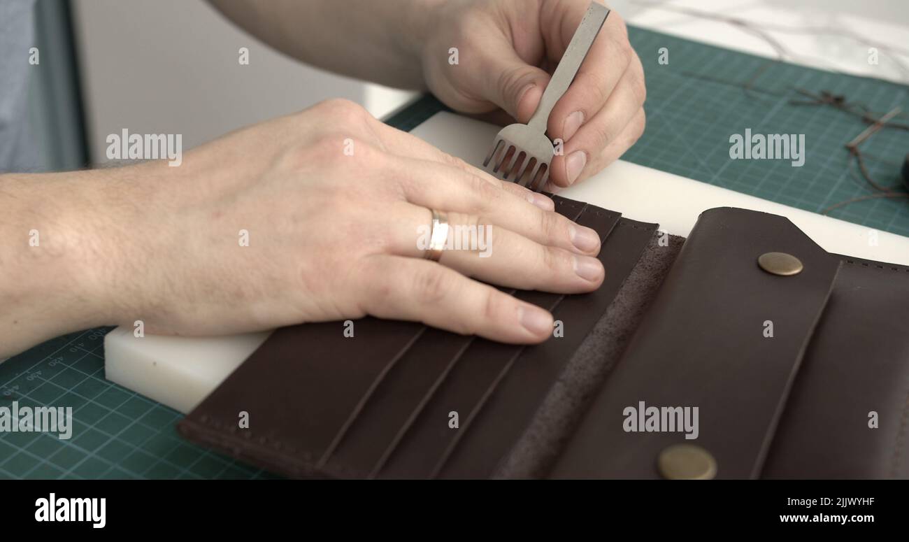Mens hand holding a hammer and hole punch and makes a holes for seawing ...