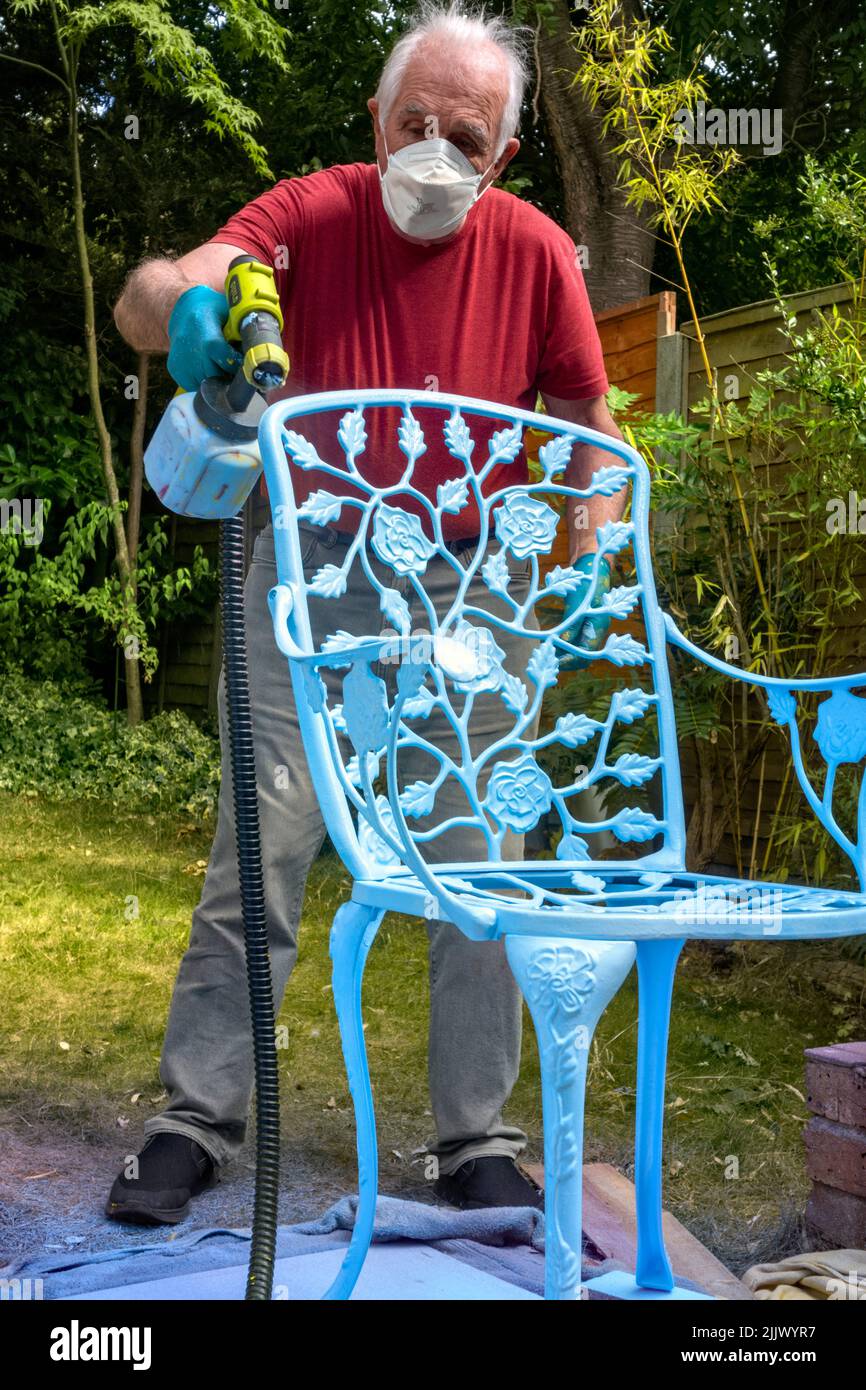 Senior male using paint spray gun to spray and upcycle wrought iron ...