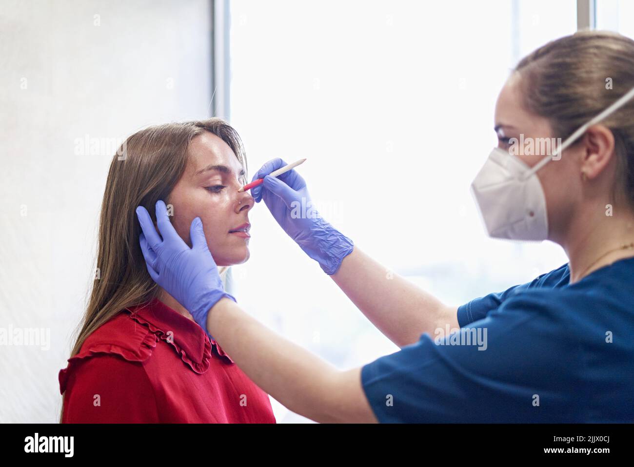 Side view of blur beautician in latex gloves drawing line with white ...