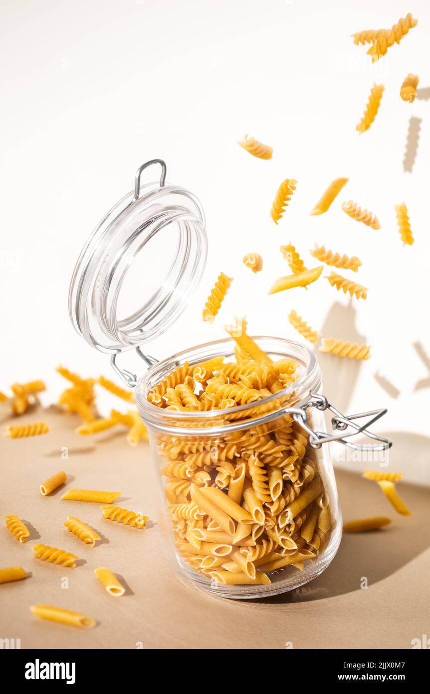 High angle of bunch of uncooked fusilli and penne pasta falling into ...