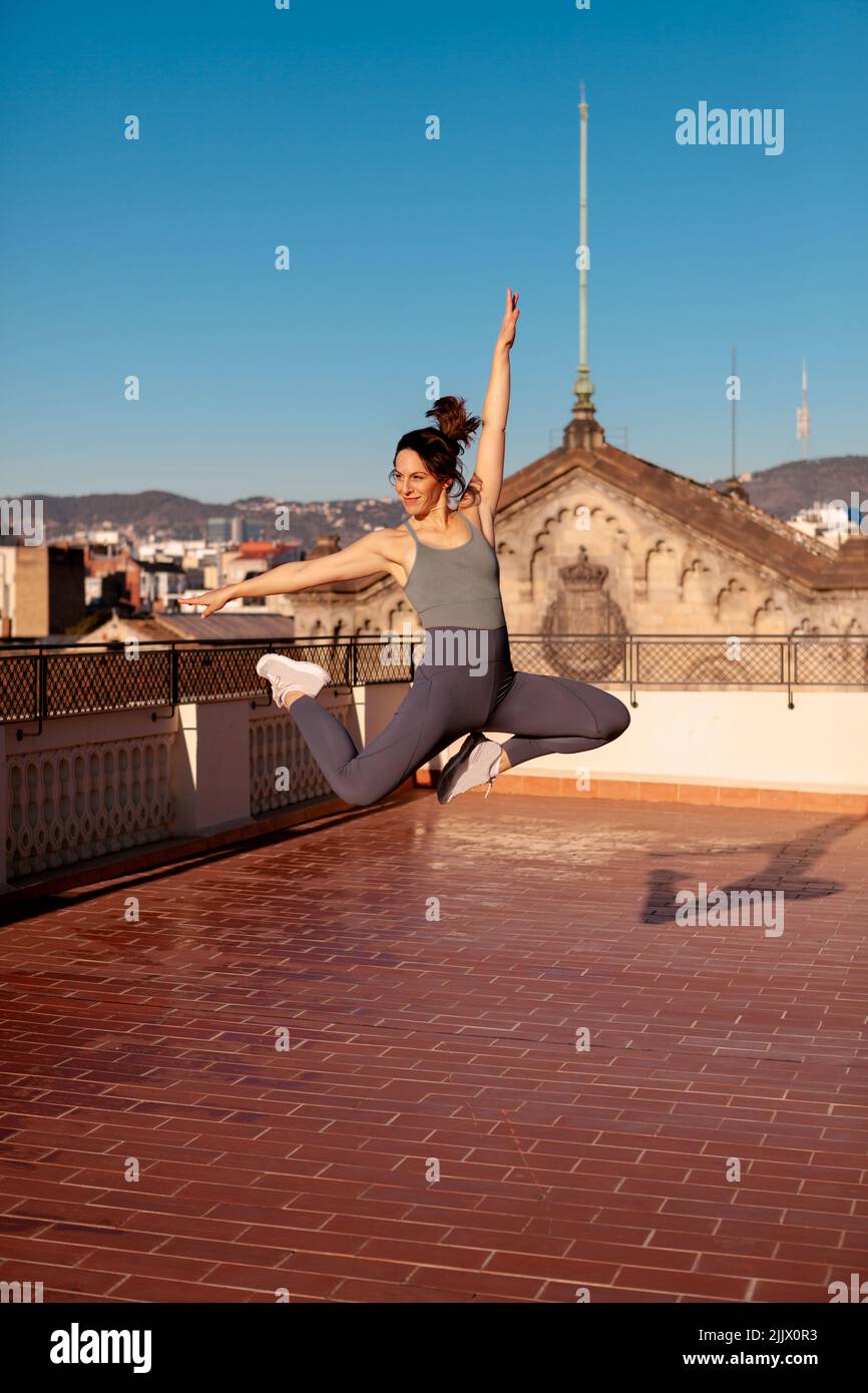 Full of active female in activewear jumping with raised arm while ...