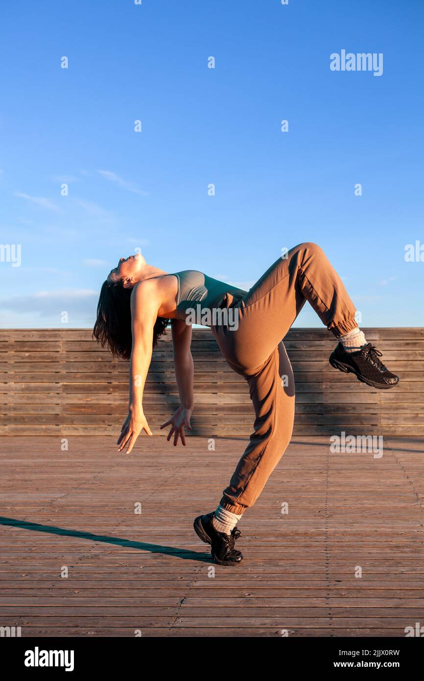 Full body of active female in sportswear bending back while warming up ...