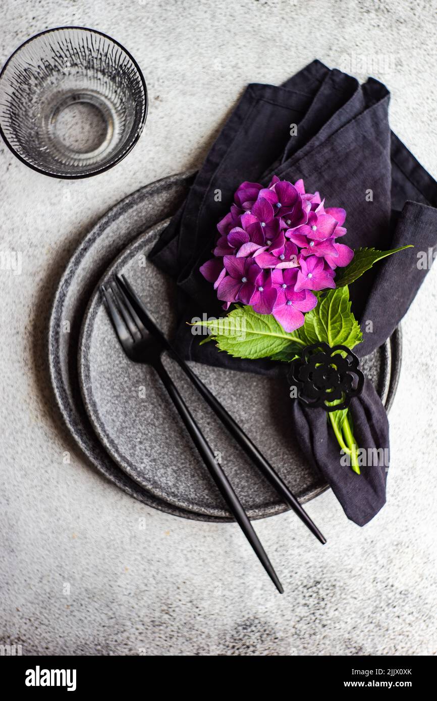Minimalist cutlery set with purple hydrangea flowers on dark concrete ...