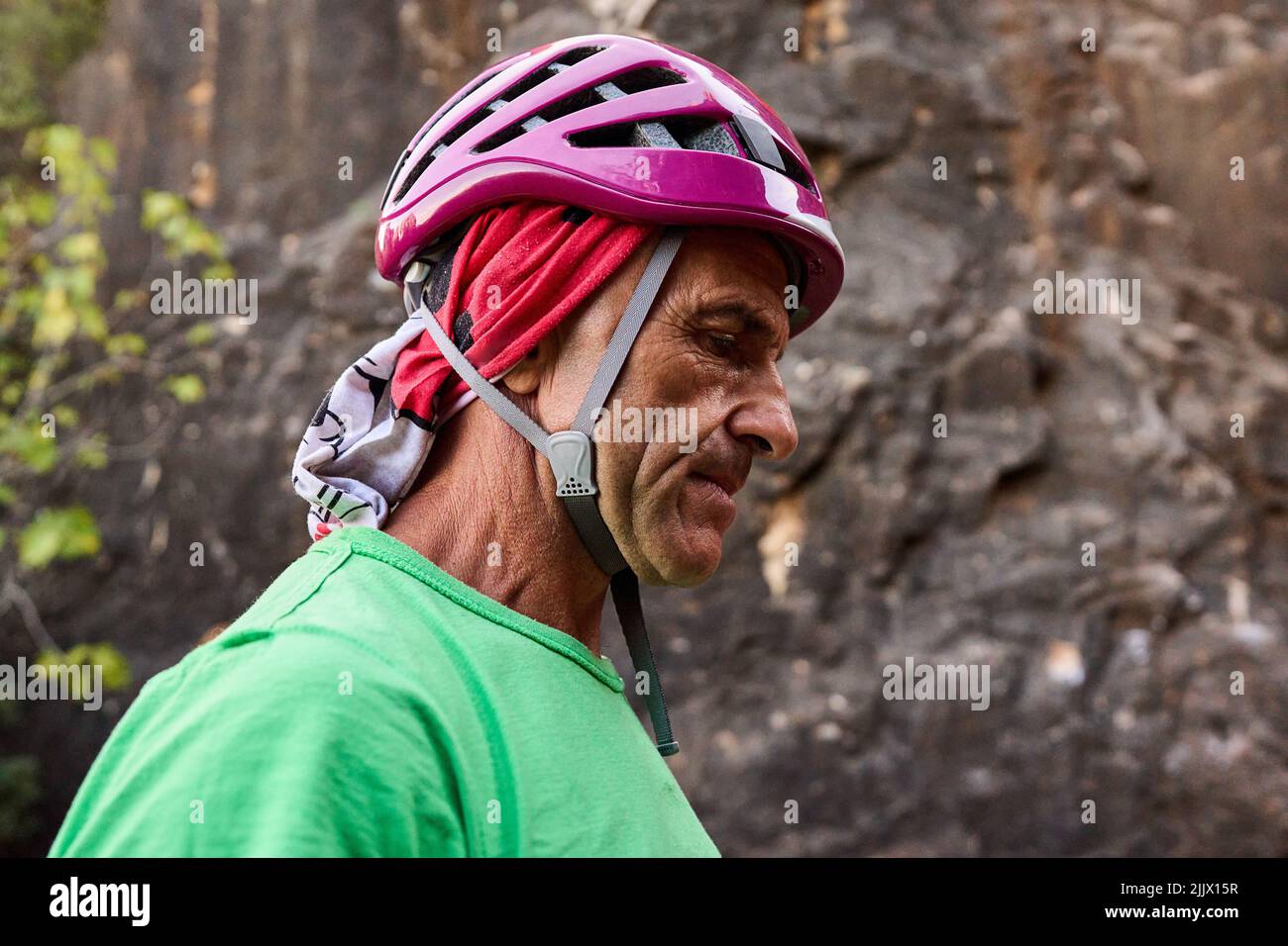 Closeup of senior male climber wearing safety helmet looking down while ...