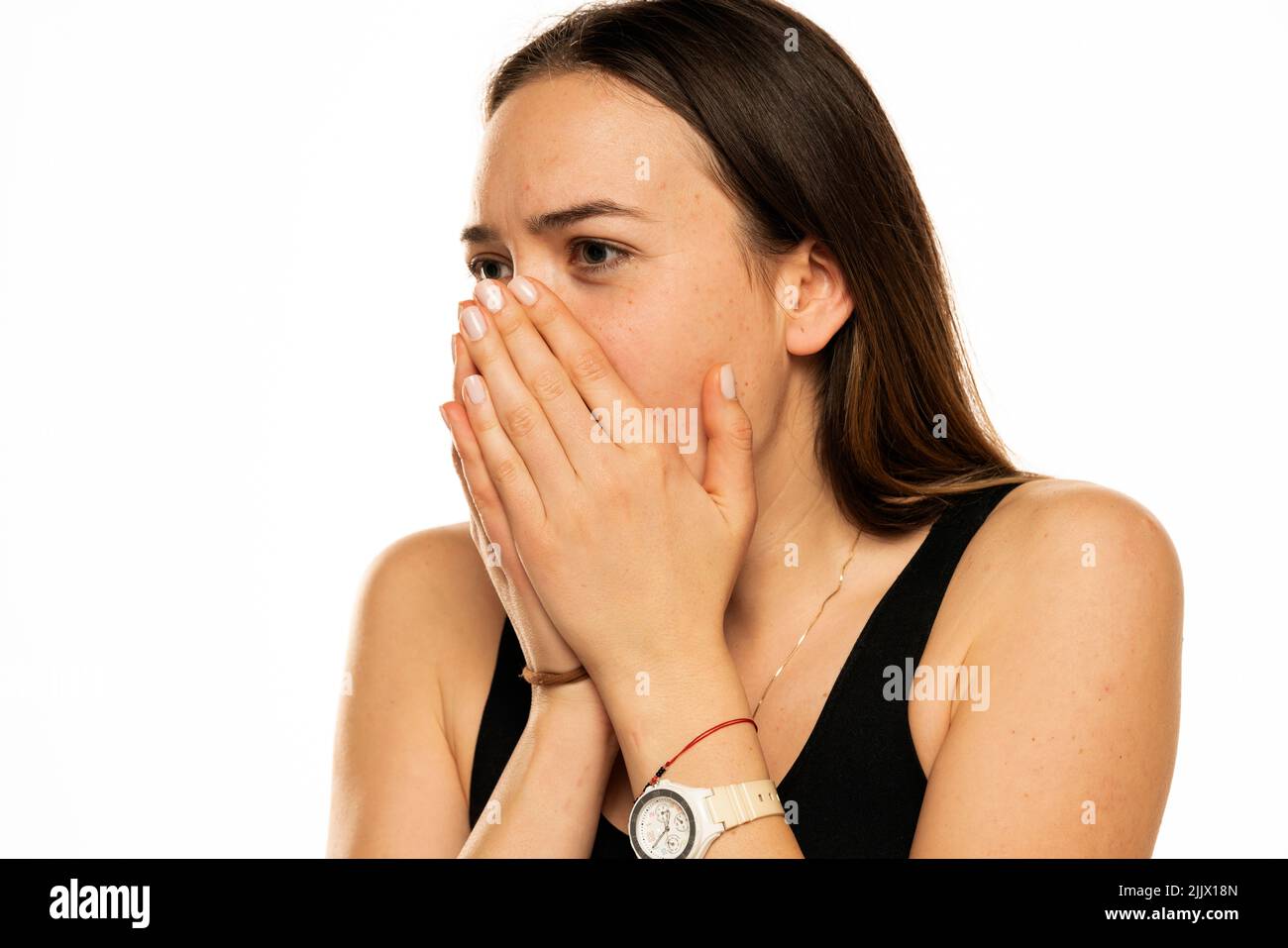 Woman in shock covers her mouth with her hands on a white background ...