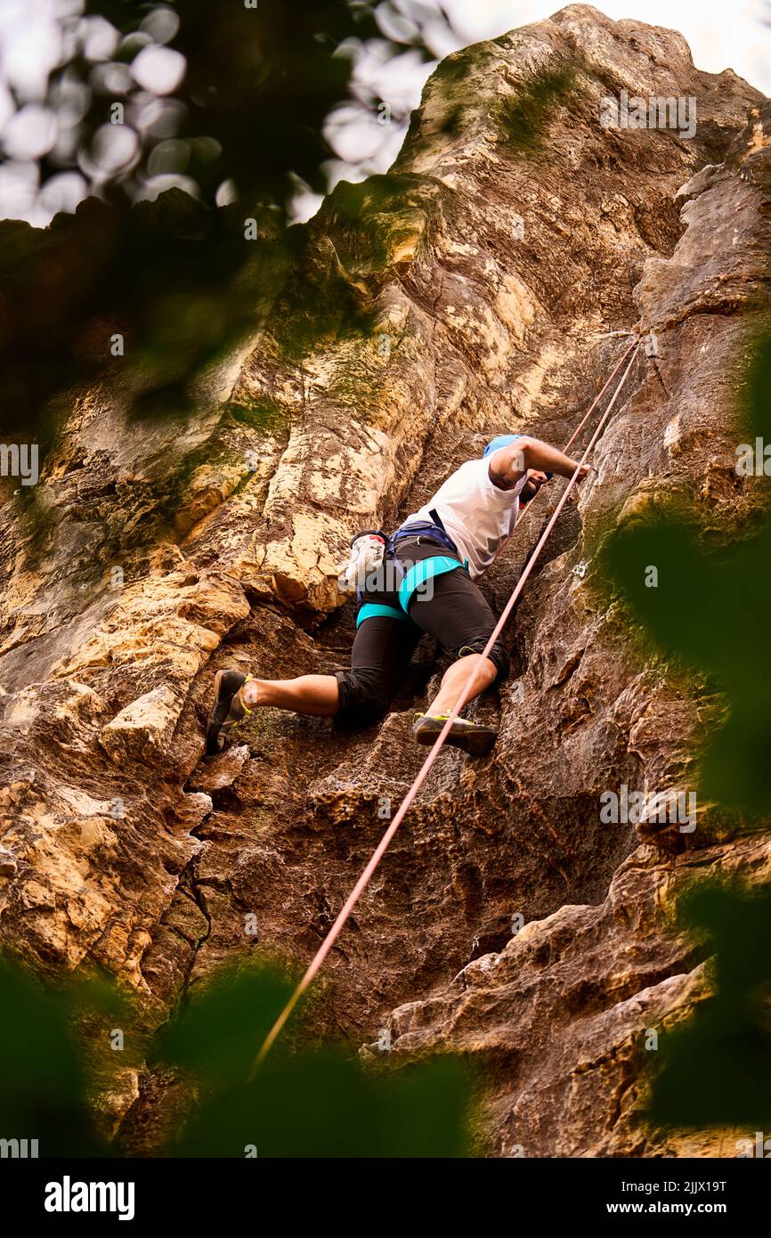 Low angle full body of active man climbing on rocky cliff Stock Photo ...