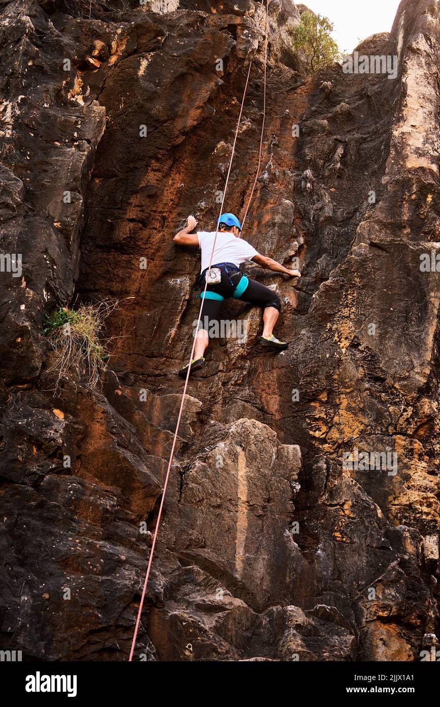 Low angle full body of active man climbing on rocky cliff Stock Photo ...