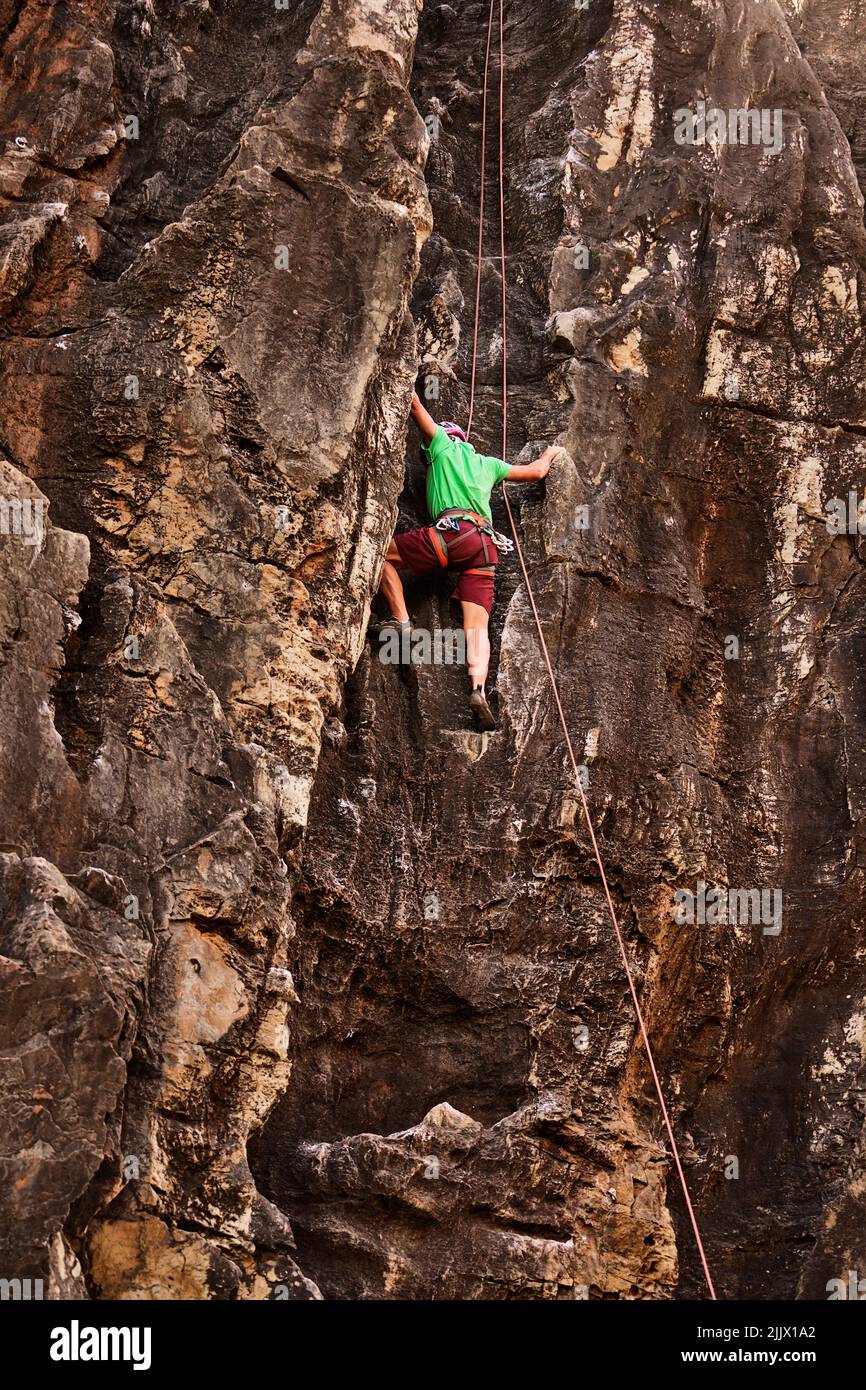 Low angle full body of unrecognizable active fit man climbing on rocky ...