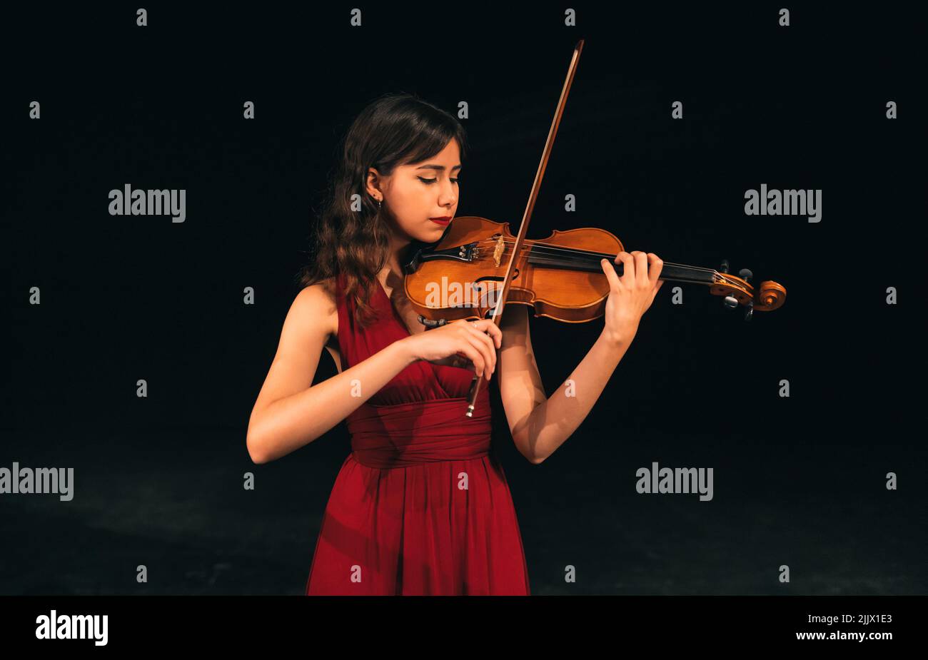 Woman in red dress playing violin with closed eyes during concert on ...