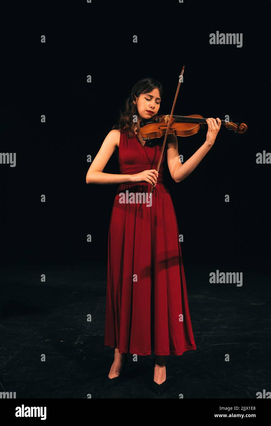 Full body Woman in red dress playing violin with closed eyes during ...