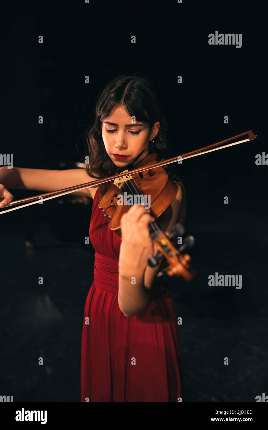 Woman in red dress playing violin with closed eyes during concert on ...
