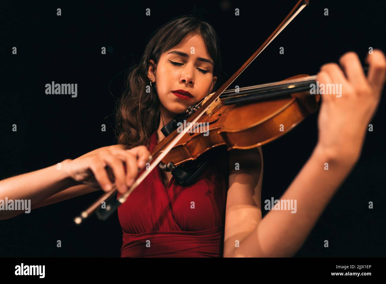 Woman in red dress playing violin with closed eyes during concert on ...