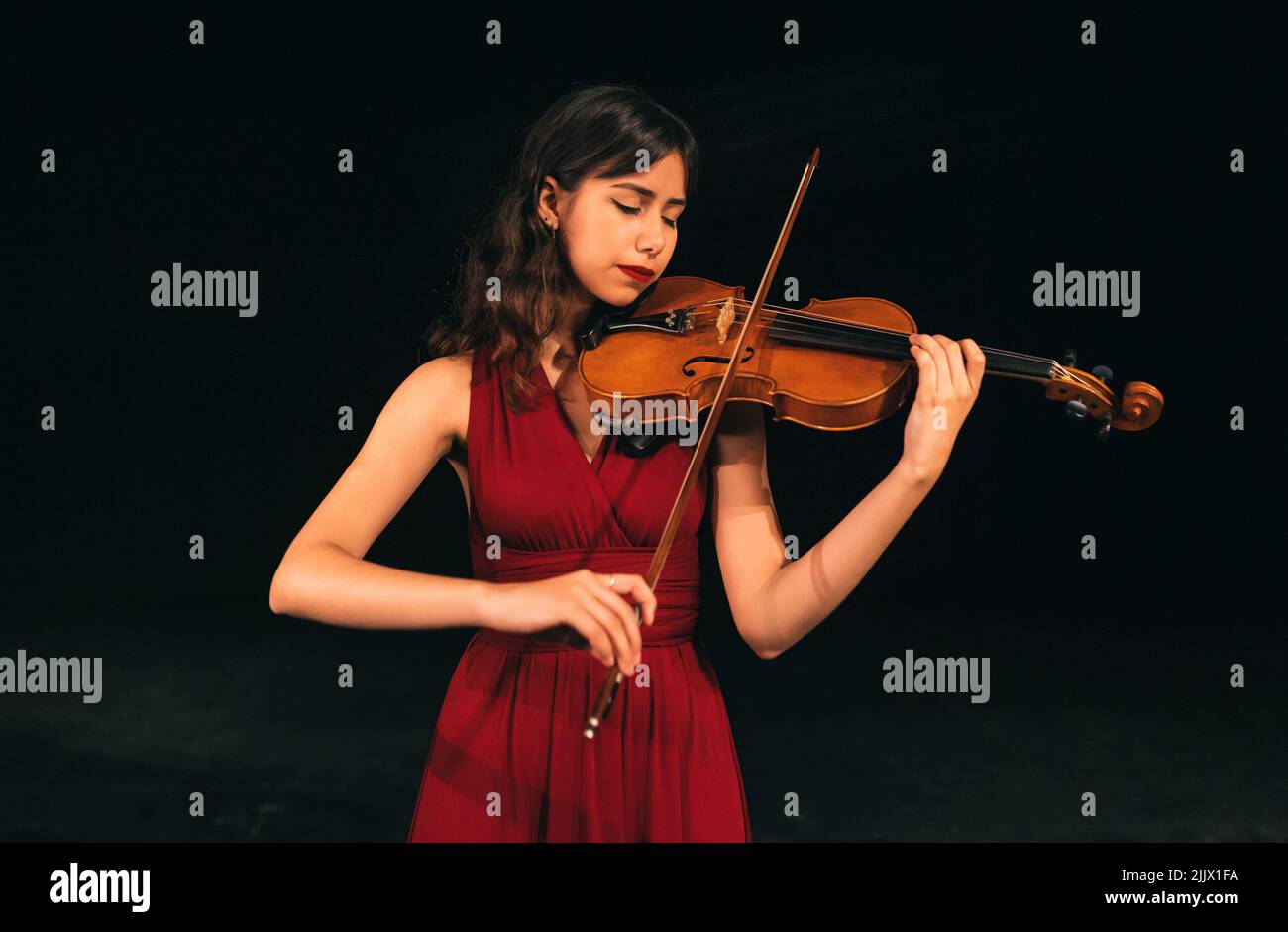 Woman in red dress playing violin with closed eyes during concert on ...