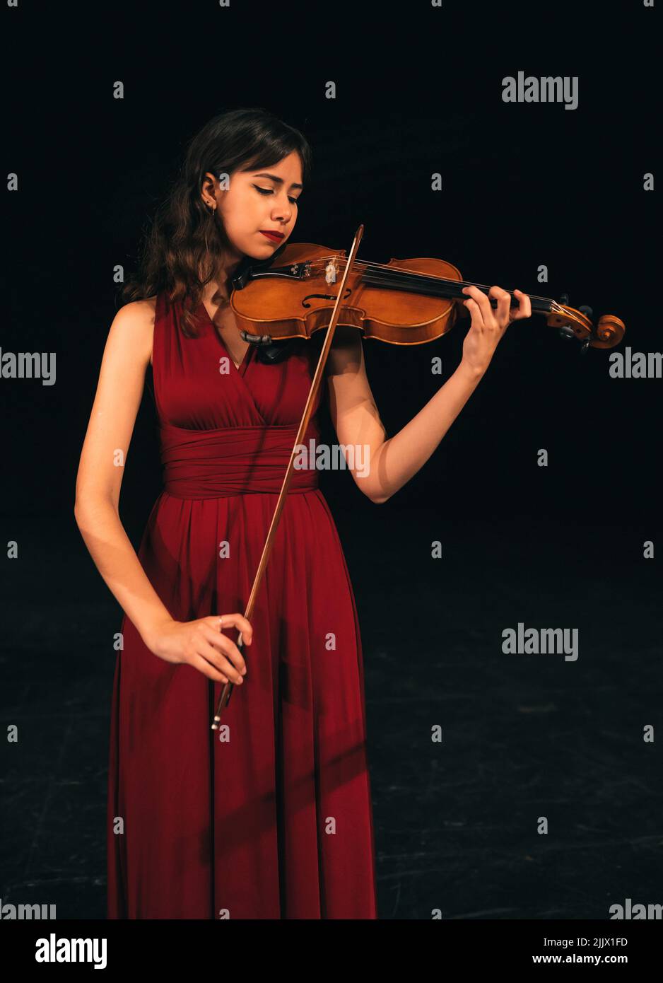 Woman in red dress playing violin with closed eyes during concert on ...