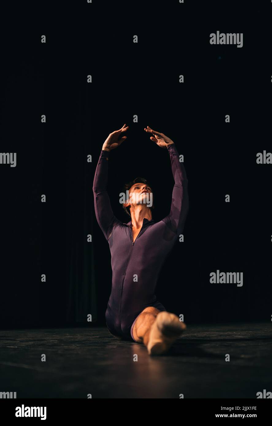 Full body male ballet dancers doing split and stretching on dark stage ...