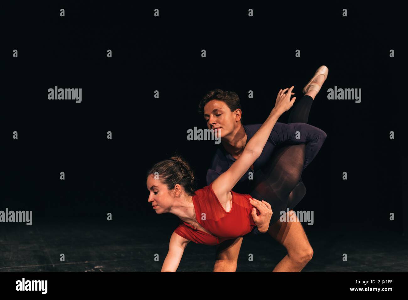 Danseur lifting ballerina while dancing on dark stage during rehearsal ...