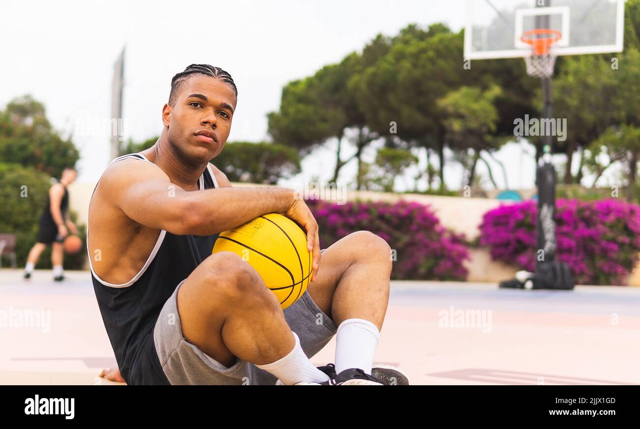 Young Hispanic sportsman with ball sitting on ground and looking at ...