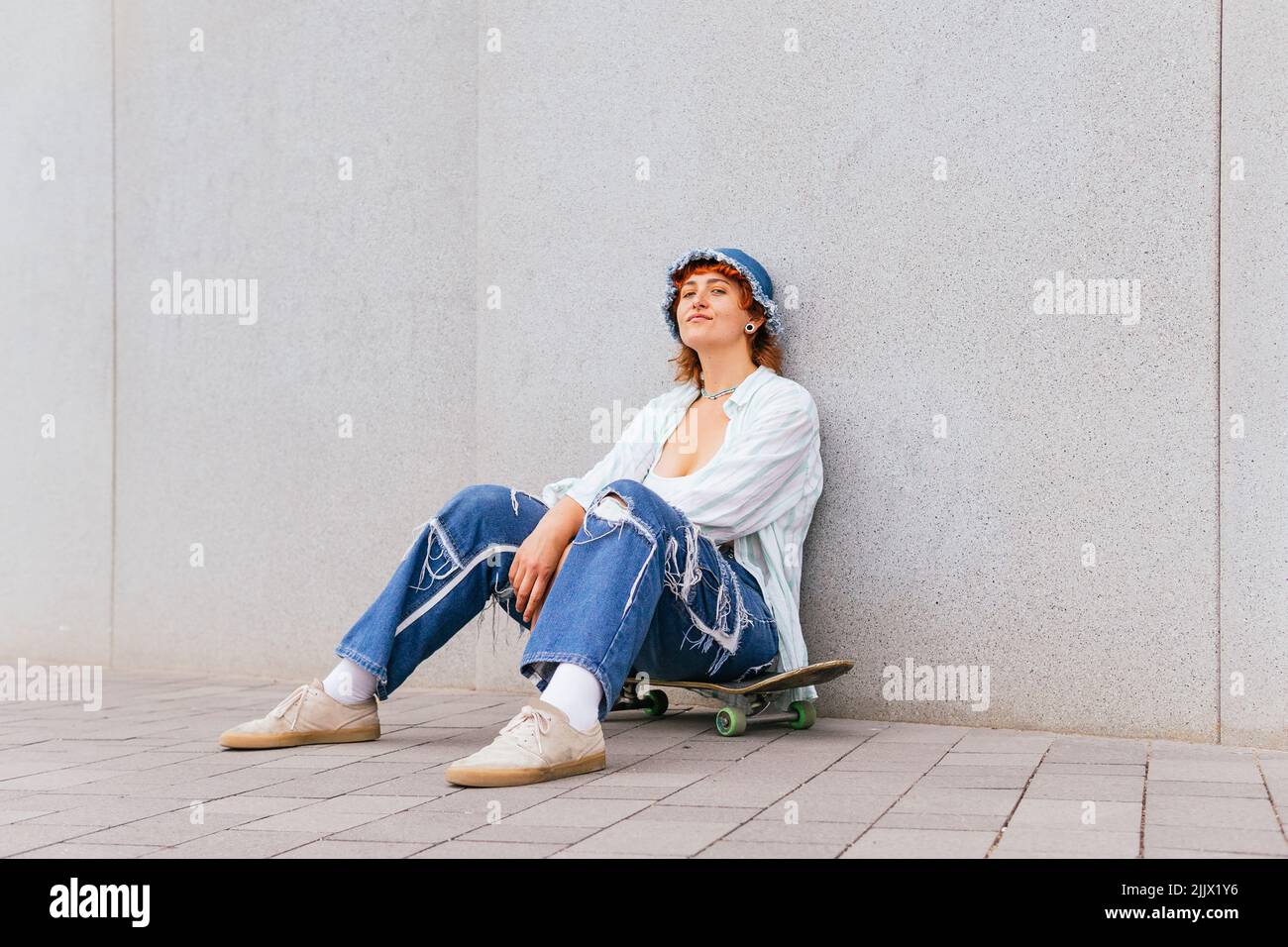 Full body of smiling female in casual wear sitting on skateboard ...