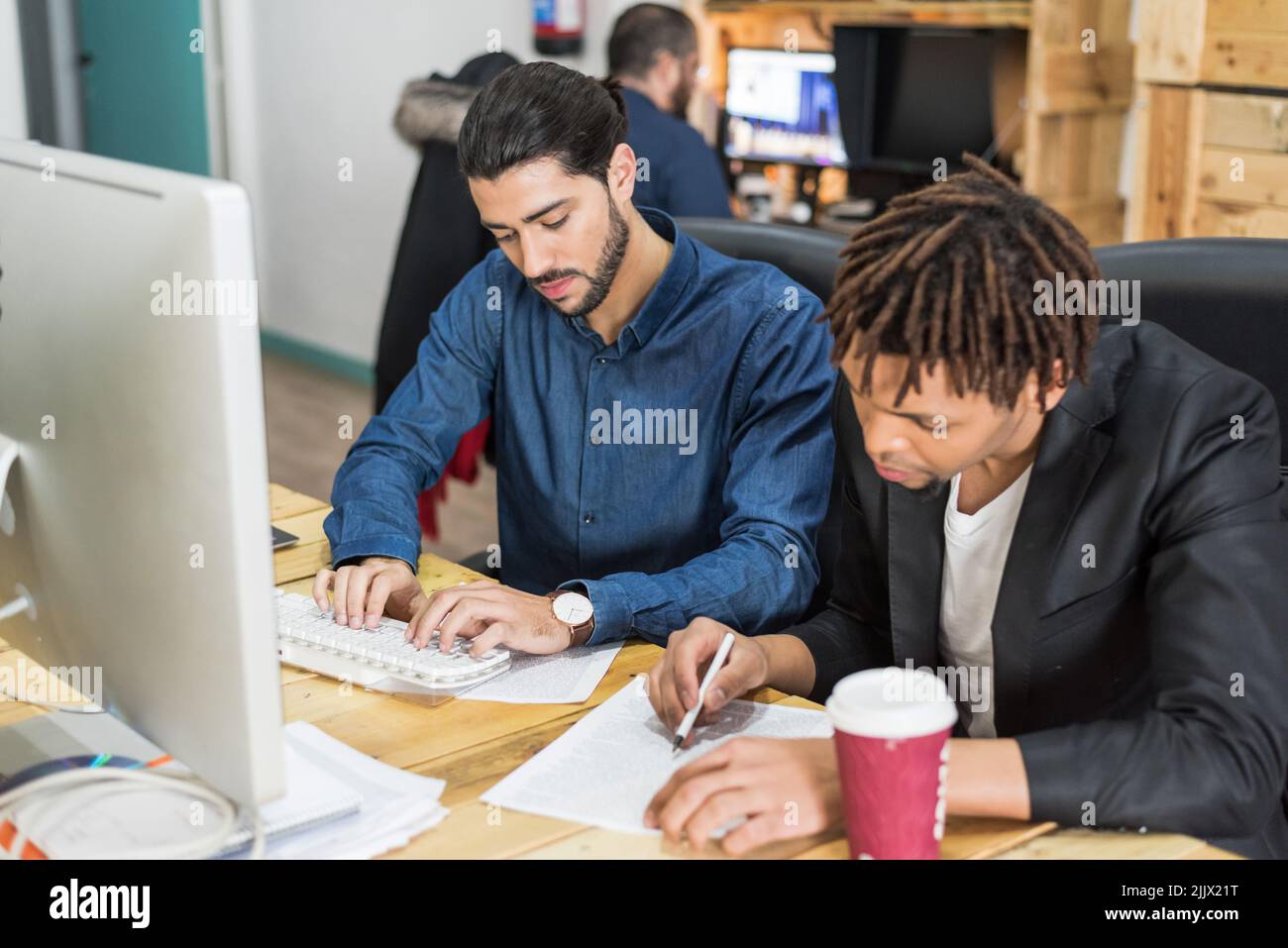 Concentrated multiracial male coworkers typing on computer and writing ...