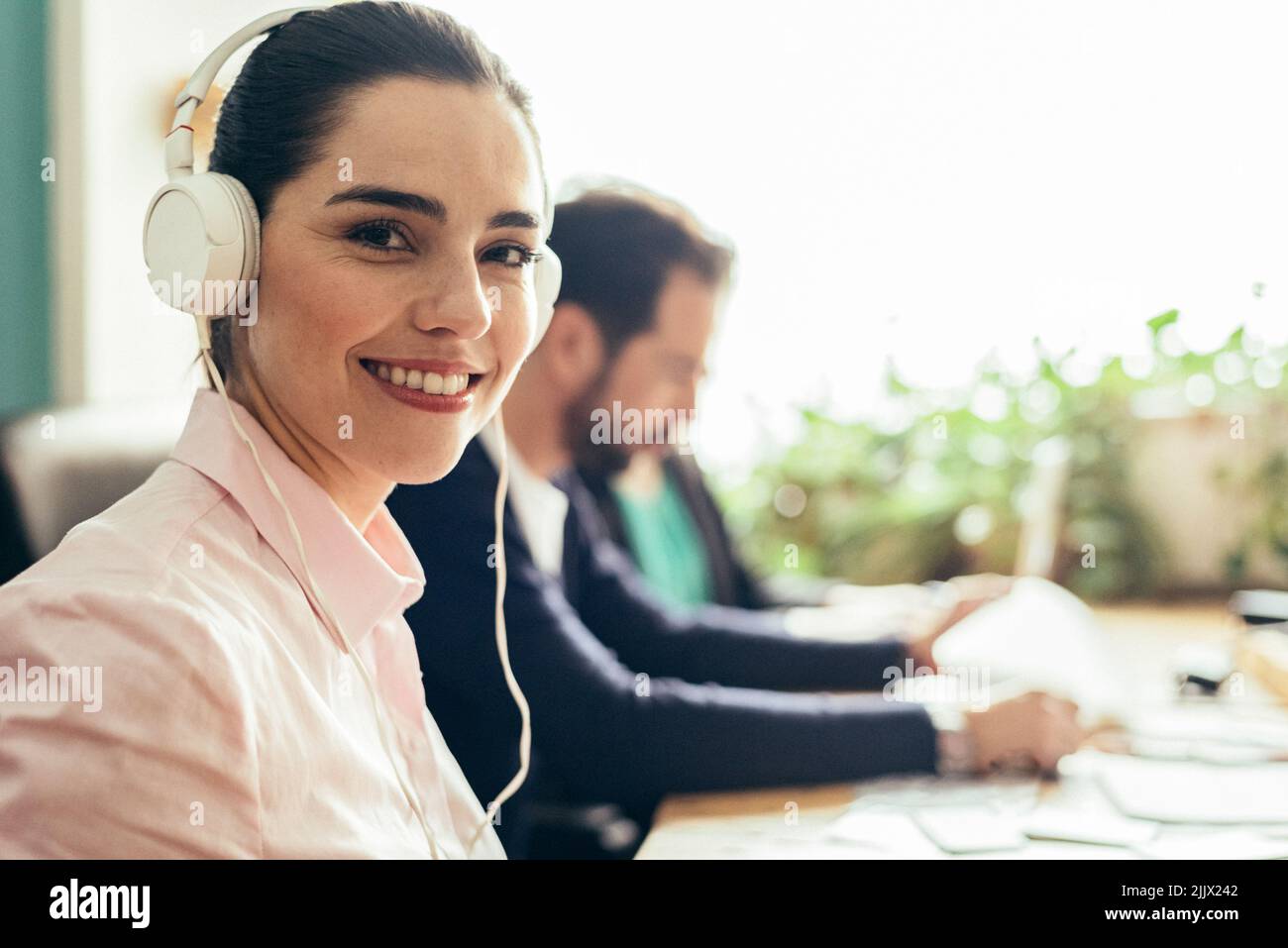 Side view of content female worker looking at camera and listening to ...