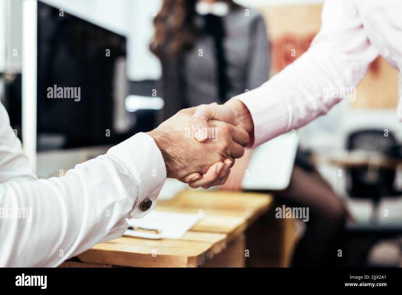 Crop anonymous workers in formal wear shaking hands near wooden table ...