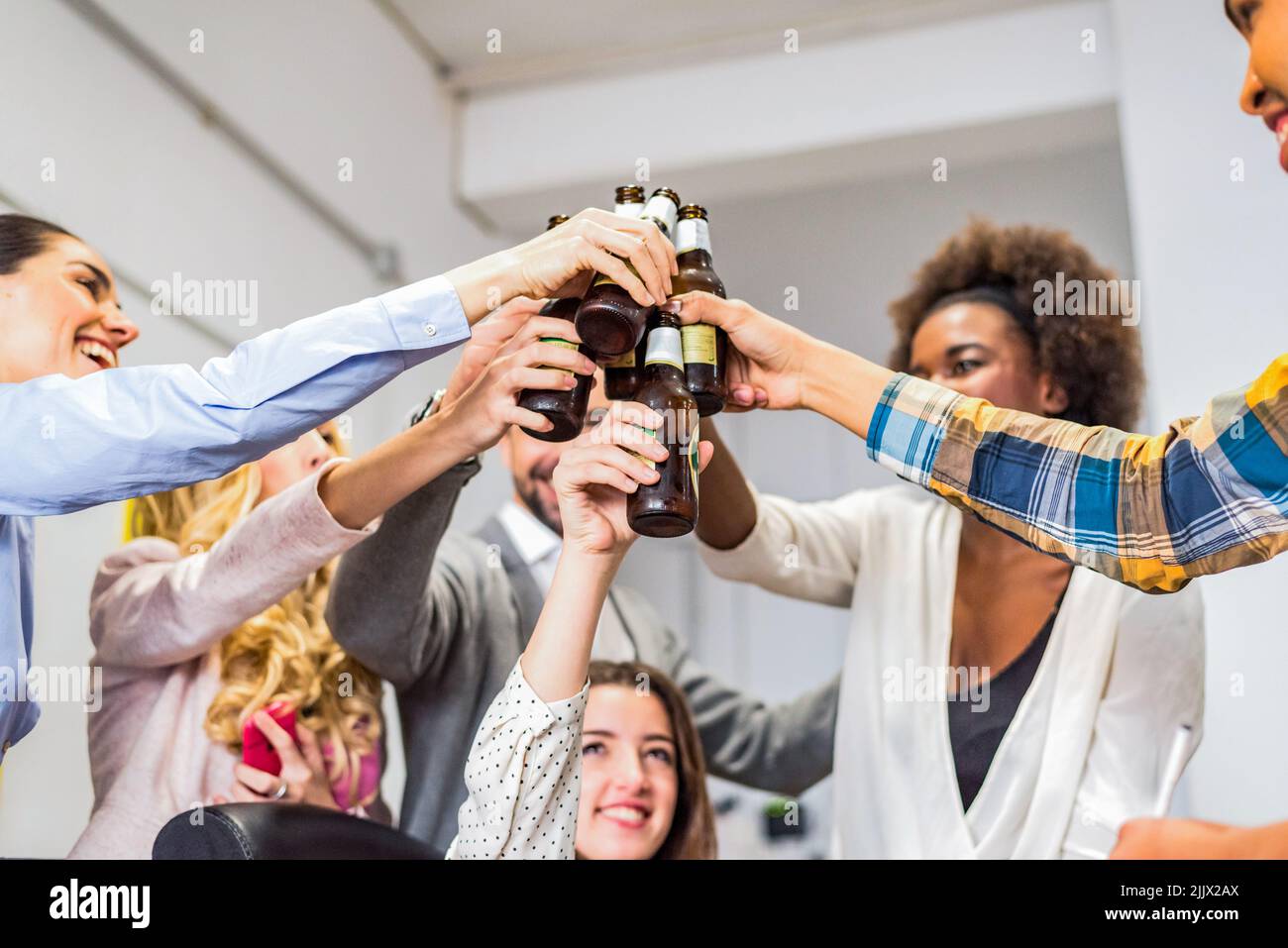 Group of happy multiethnic coworkers in stylish wear clinking bottles ...