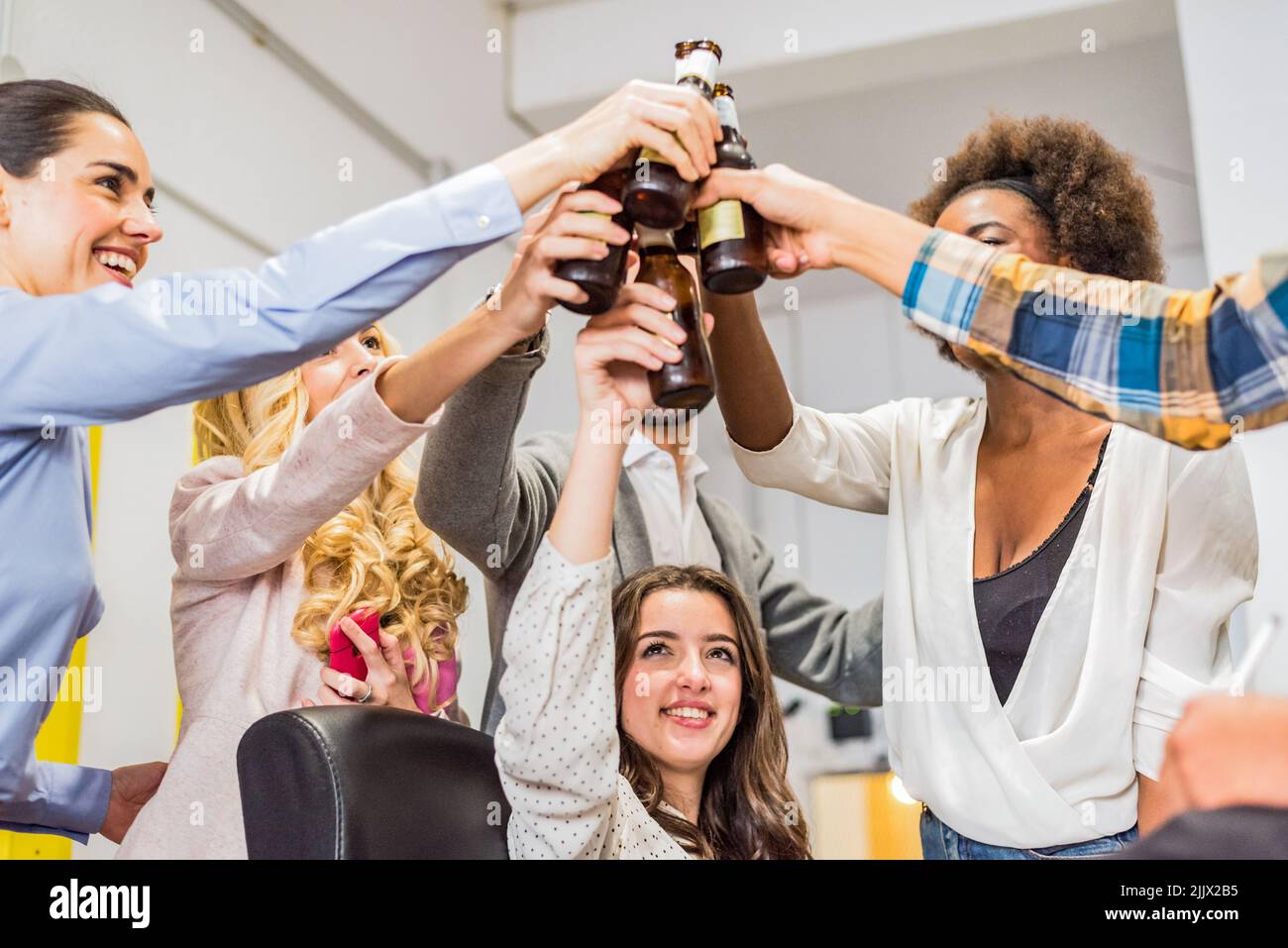 Group of happy multiethnic coworkers in stylish wear clinking bottles ...