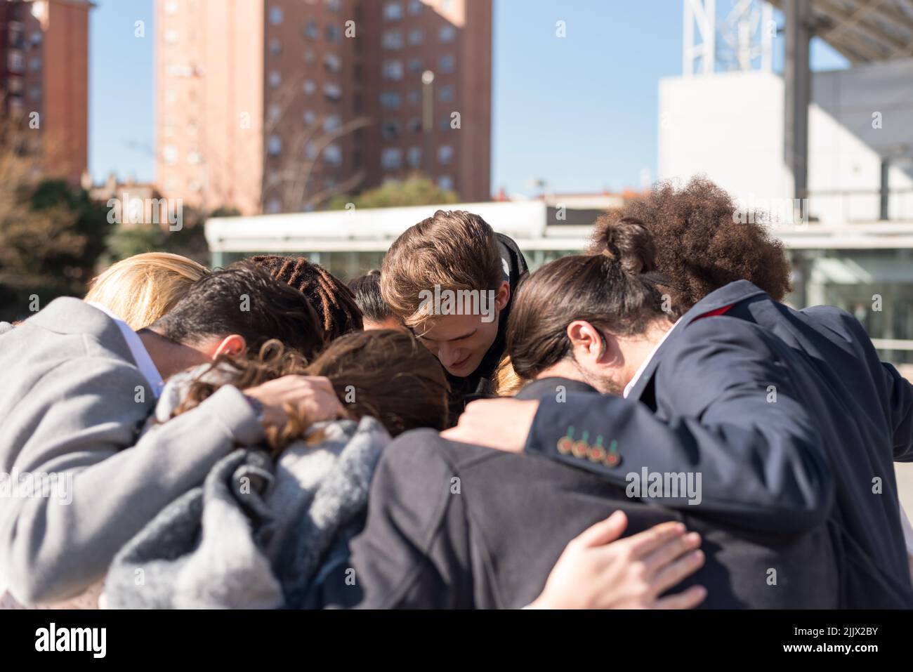 Coworkers in formal wear standing in circle and hugging each other ...
