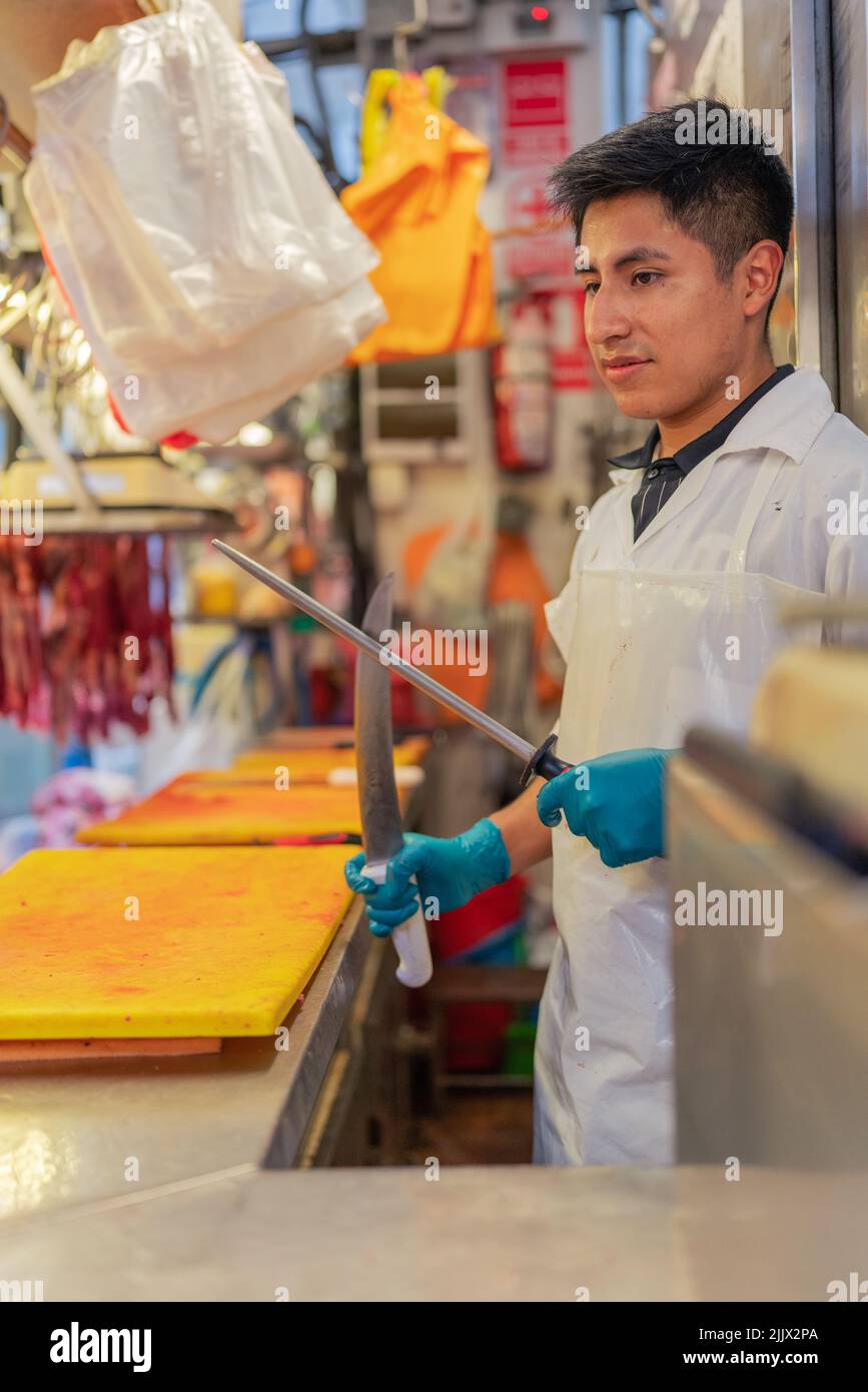 Hispanic man in white robe and latex gloves sharpening knife before ...