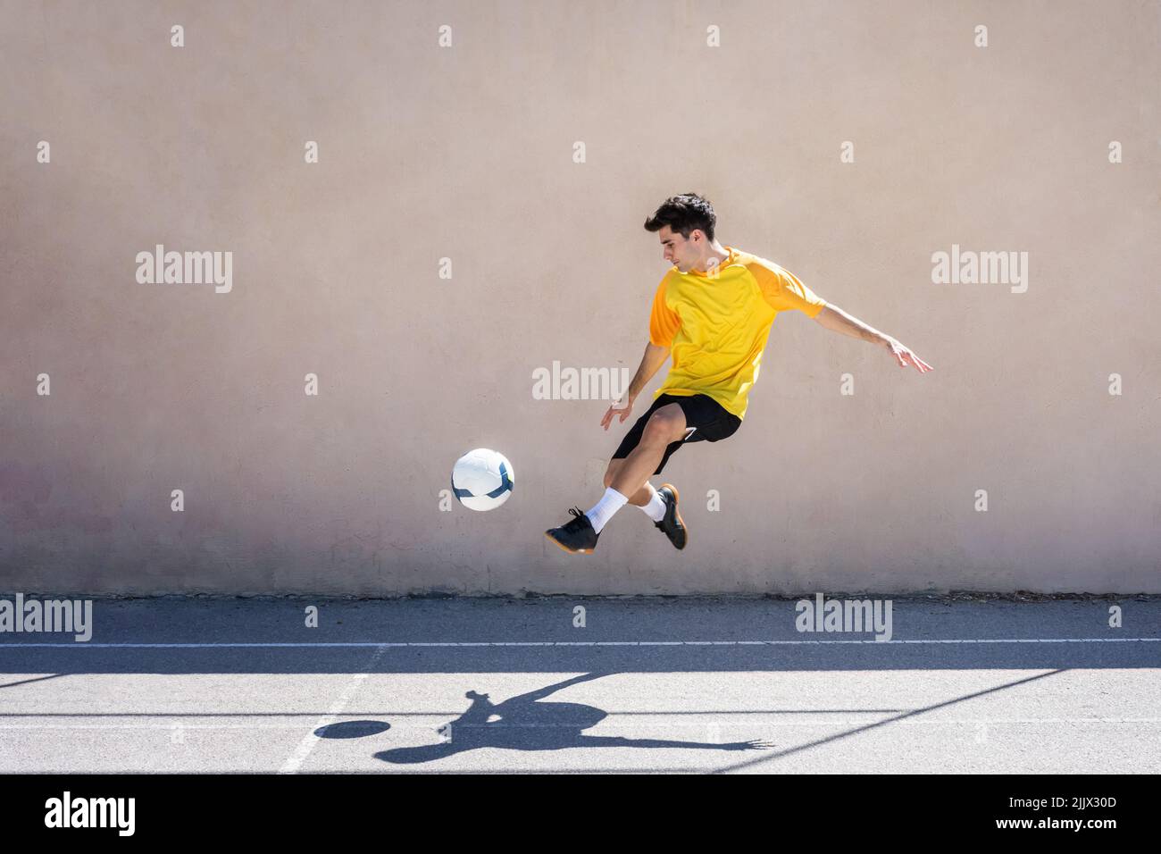 Young male player kicking football while practicing soccer against ...