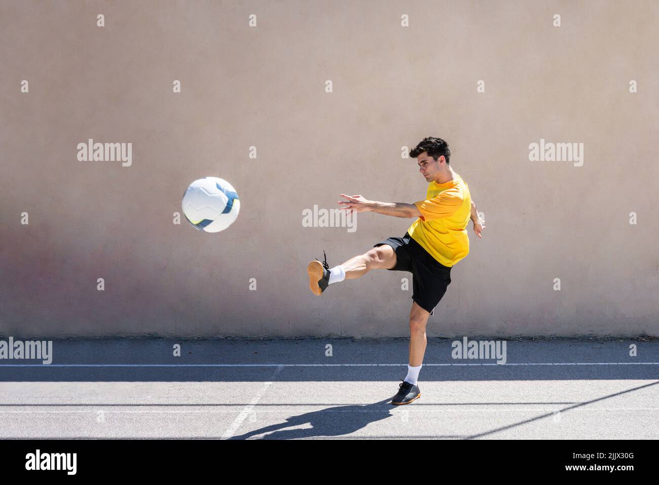 Young male player kicking football while practicing soccer against ...