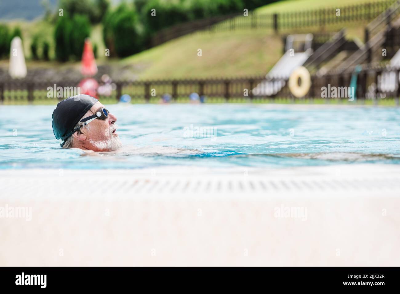 Cheerful senior male with gray hair and beard in cap and goggles doing ...