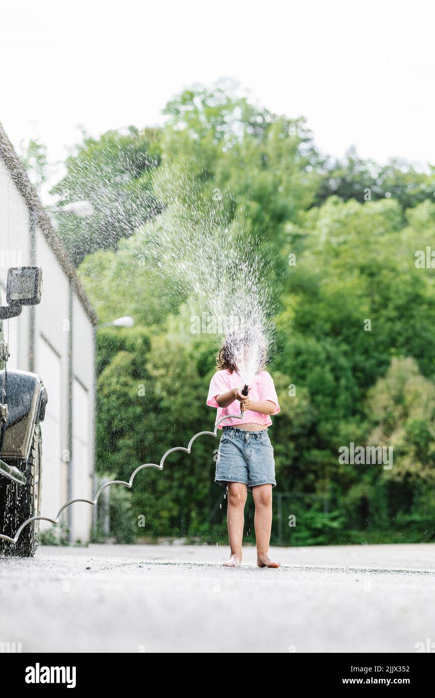 Full body of happy cute girl in casual clothes spraying with hose Stock ...