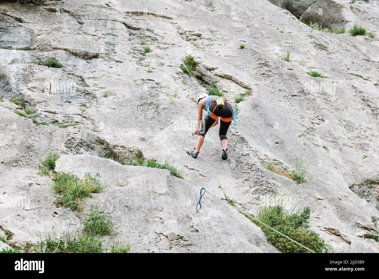 From below of female hiker wearing harness and helmet while climbing on ...