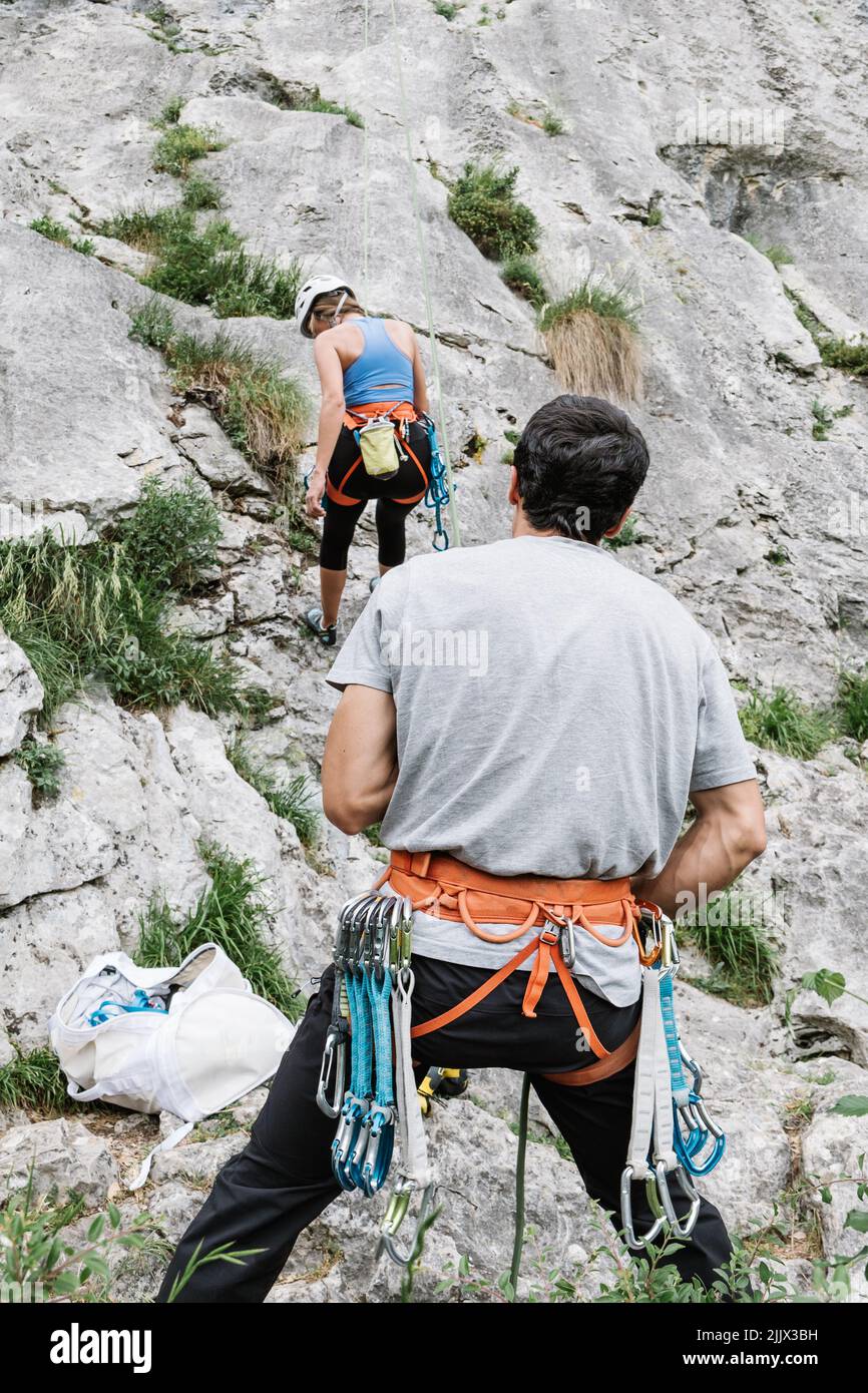Rear view of male hiker looking at female partner climbing on rocky ...