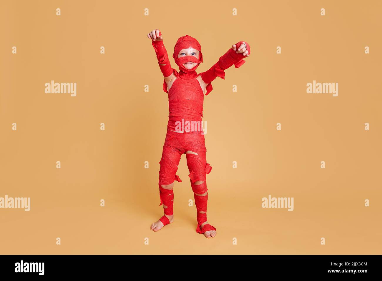 Full body of little boy in red mummy costume making face and raising ...