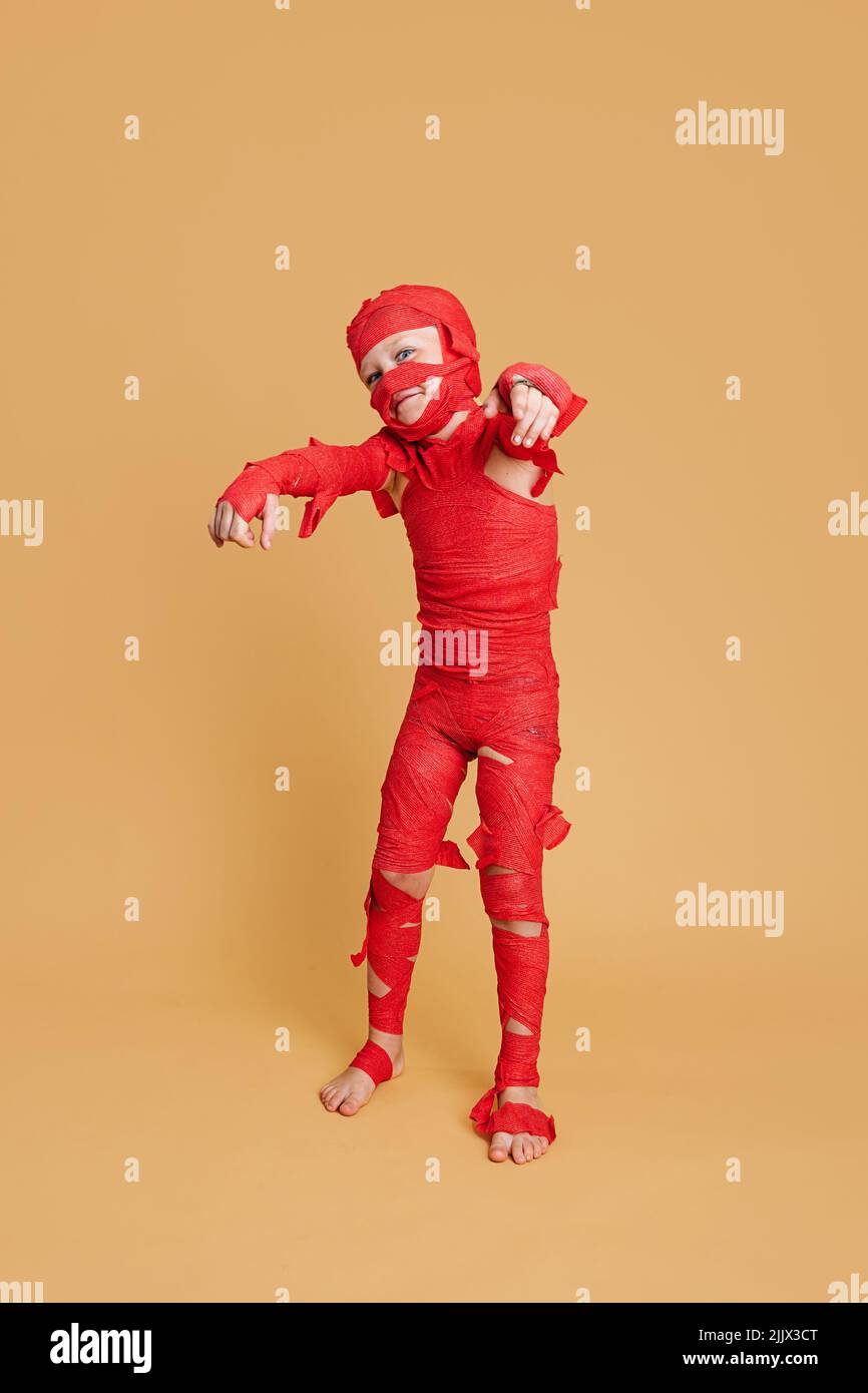 Full body of little boy in red mummy costume making face and raising ...