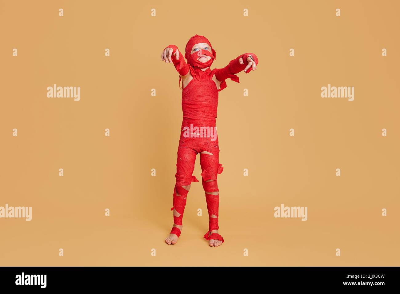 Full body of little boy in red mummy costume making face and raising ...