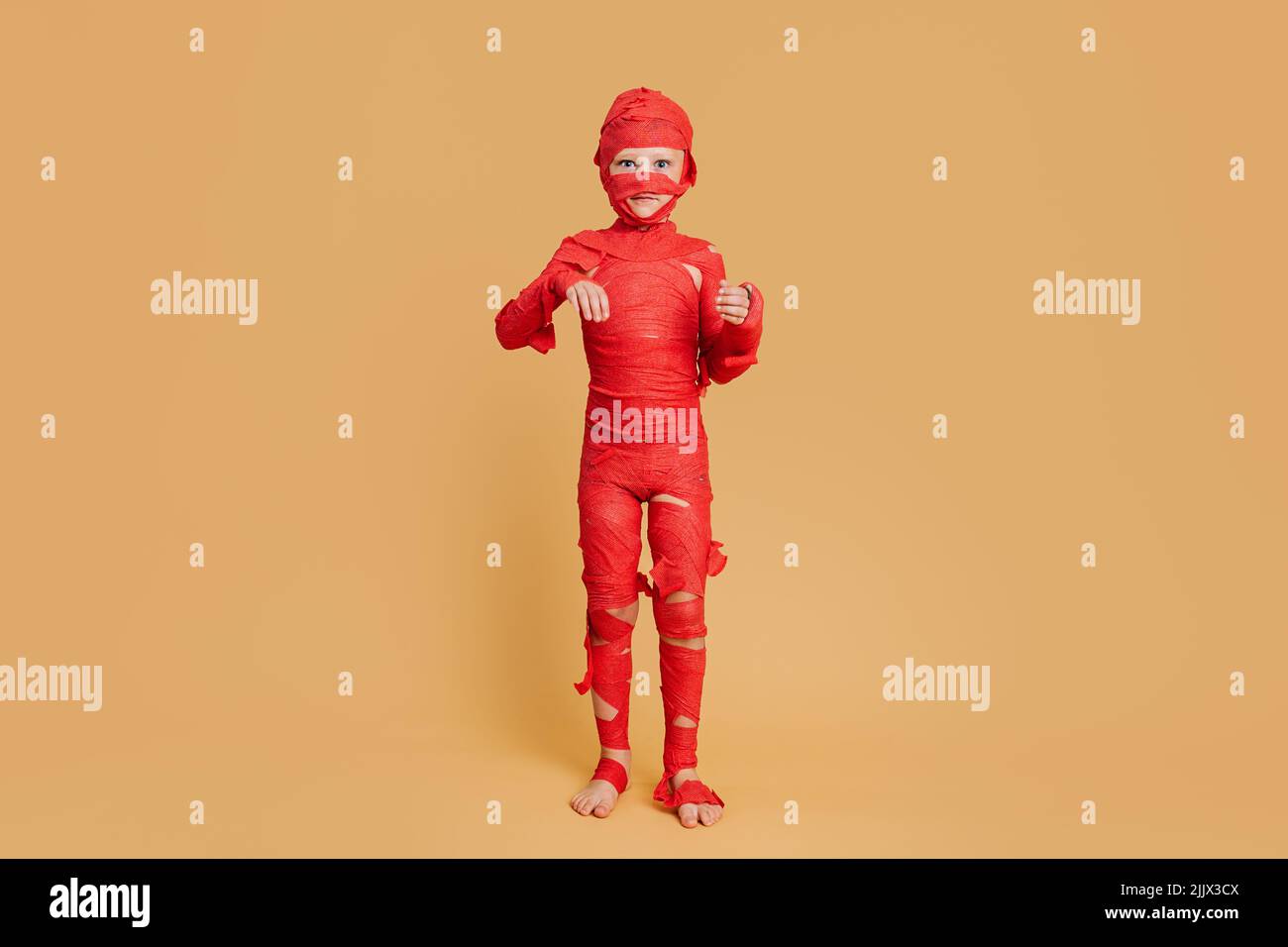 Full body of little boy in red mummy costume making face and raising ...