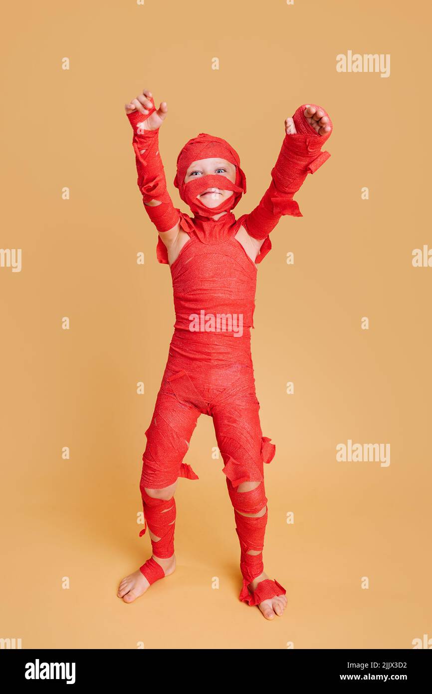 Full body of little boy in red mummy costume making face and raising ...
