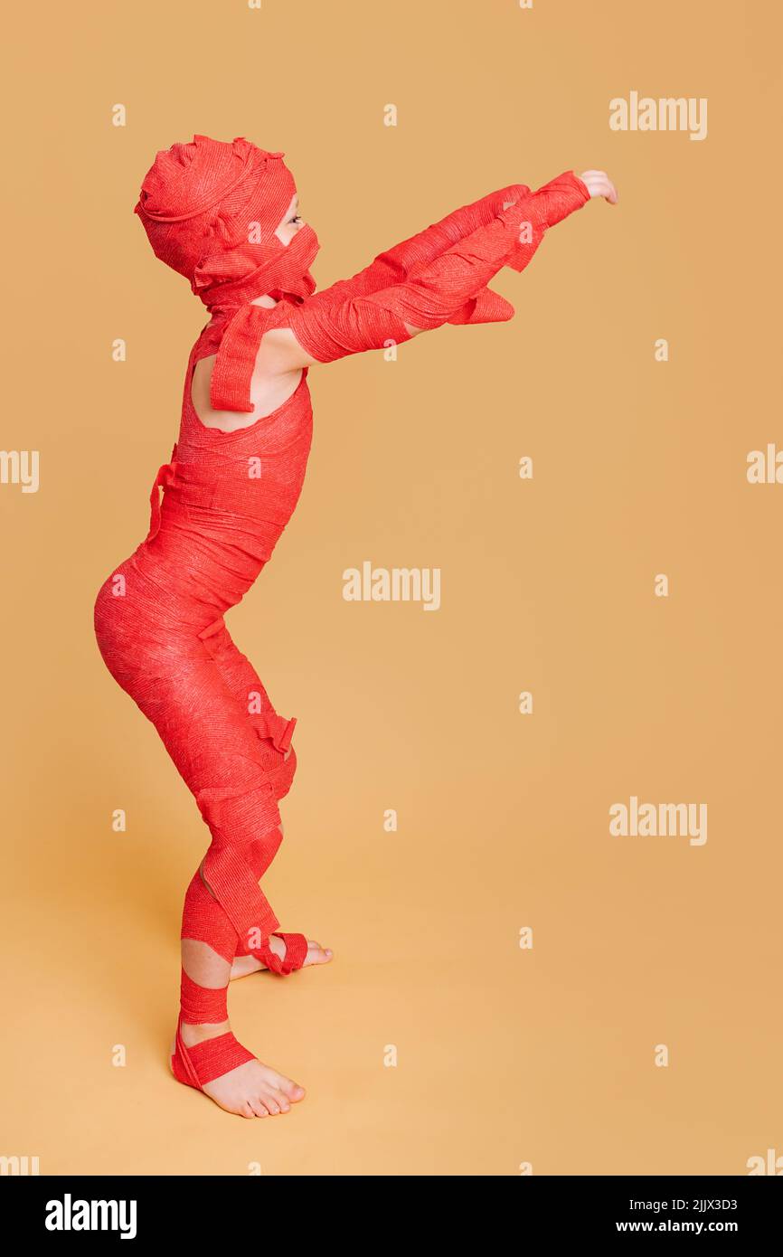 Full body side view of little boy in red mummy costume making face and ...